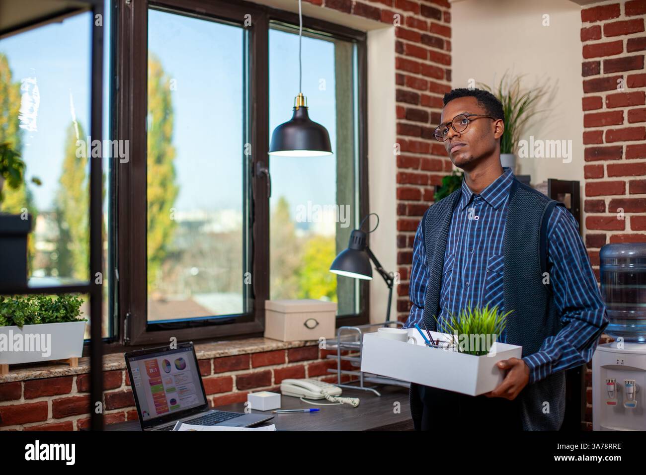 Black employee with spectacles, holding a box of work supplies ...