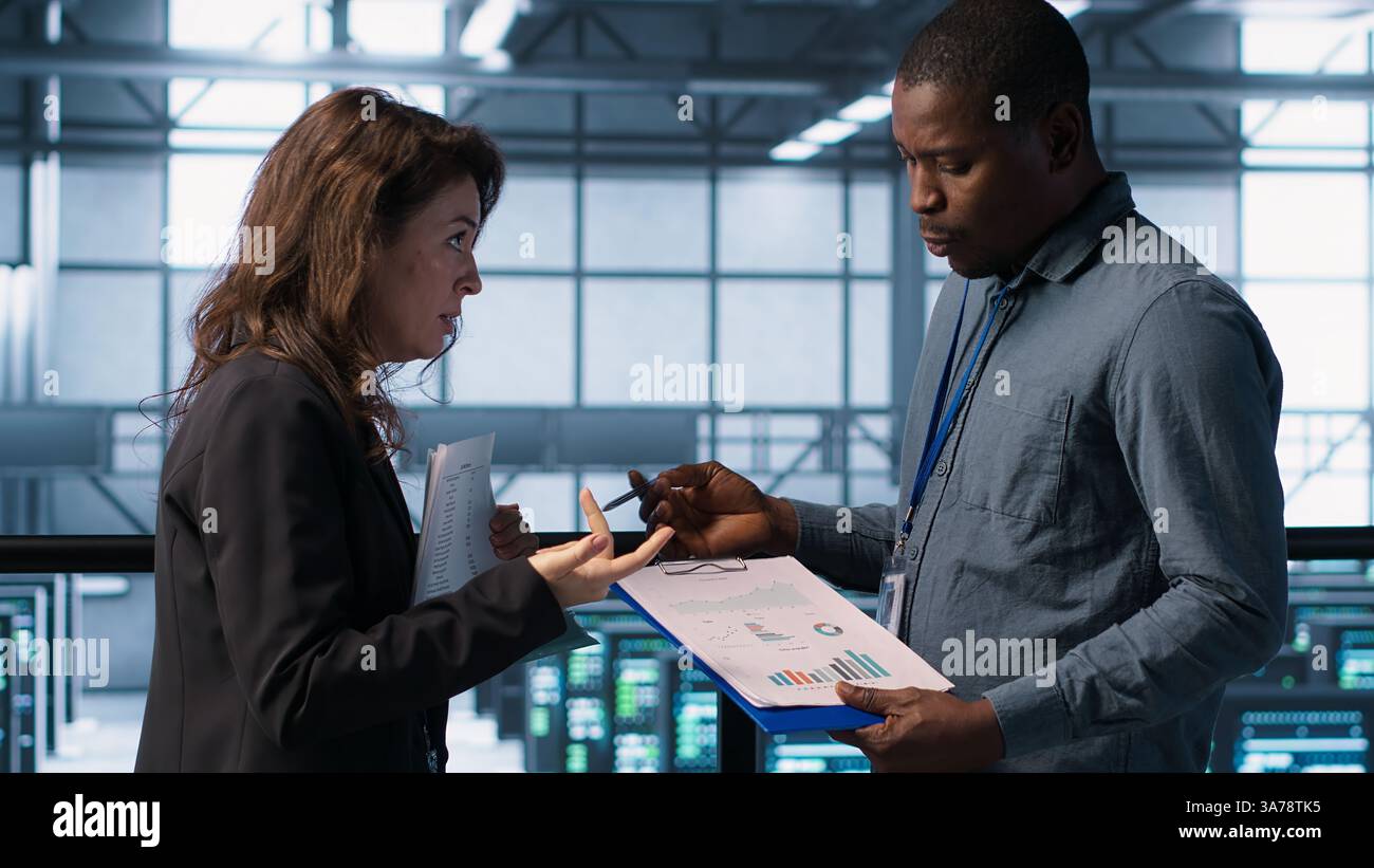 Data center team examines paperwork files in server room, reviewing ...