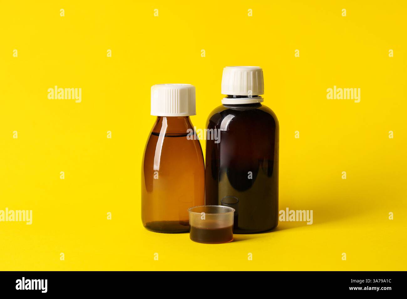 Bottles and measuring cup of cough syrup on yellow background Stock ...
