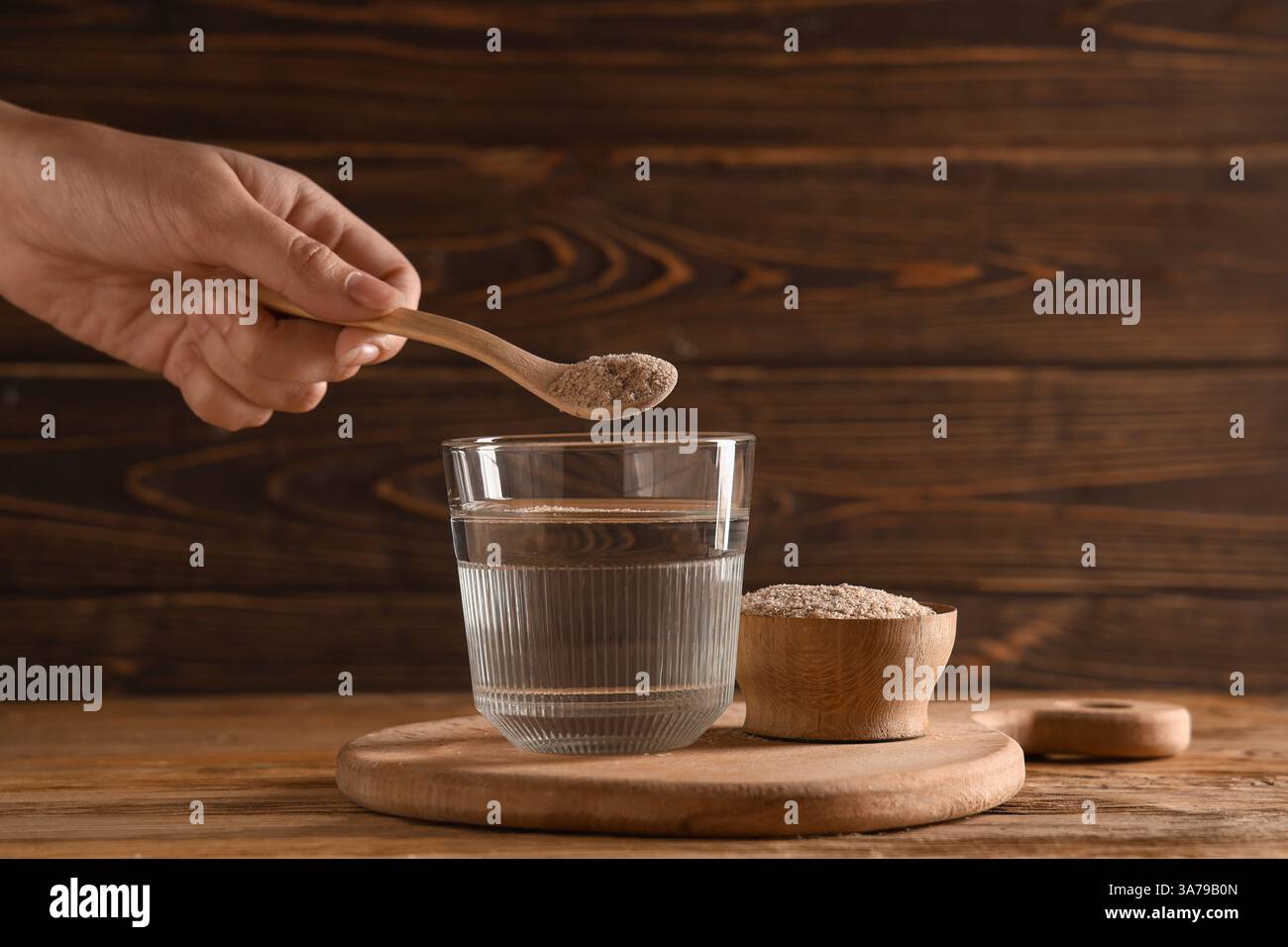 Female hand adding psyllium husk into glass of water on wooden ...