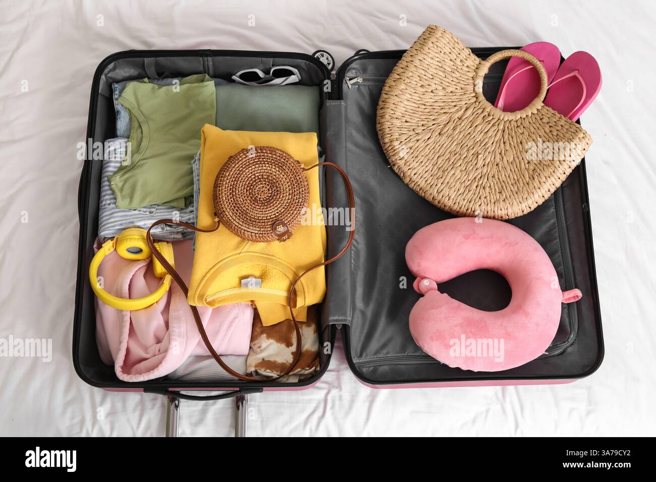 Unpacked suitcase with clothes and travelling accessories on bed in ...