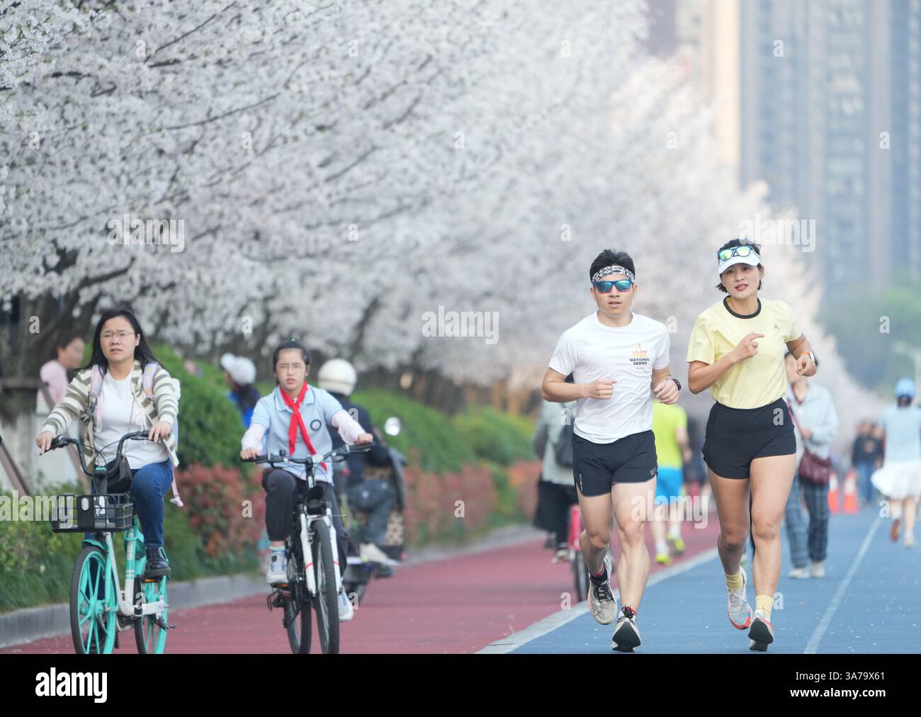 Beijing, China's Zhejiang Province. 26th Mar, 2025. People run and bike along a track flanked by ...