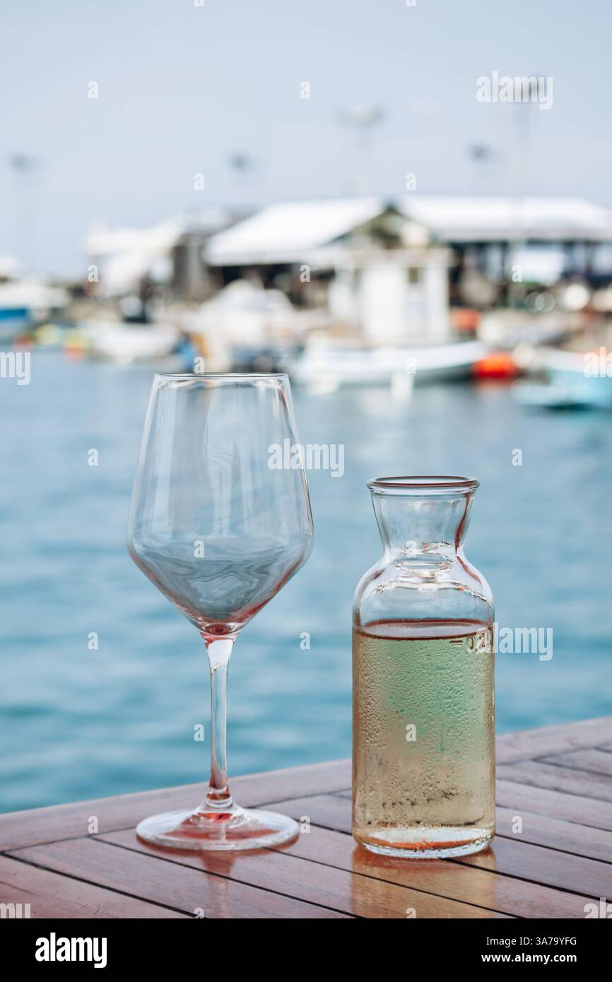 A glass and a small carafe of white wine facing the blue sea in Koper ...