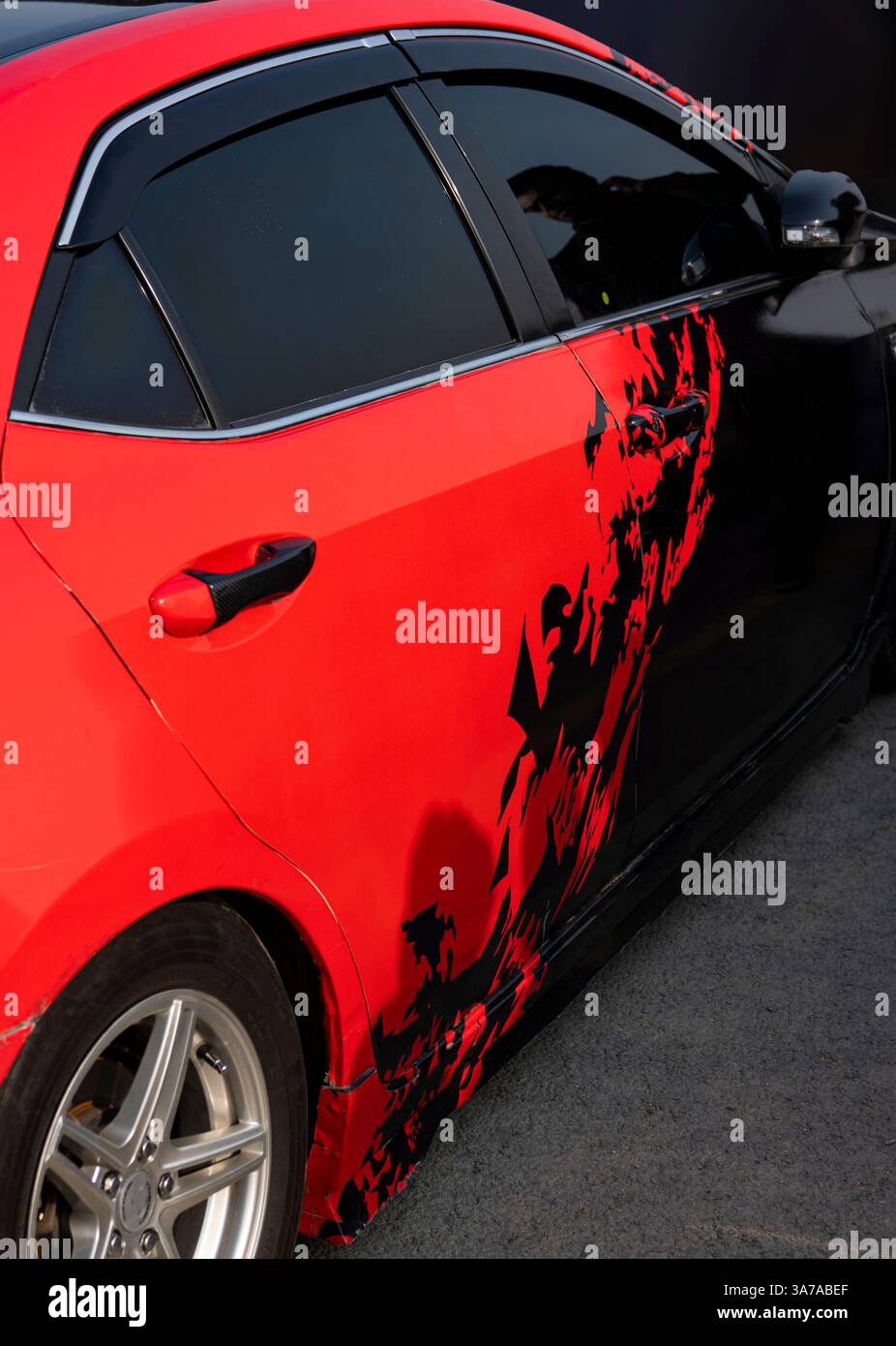 A striking red and black car featuring vibrant sticker designs along ...