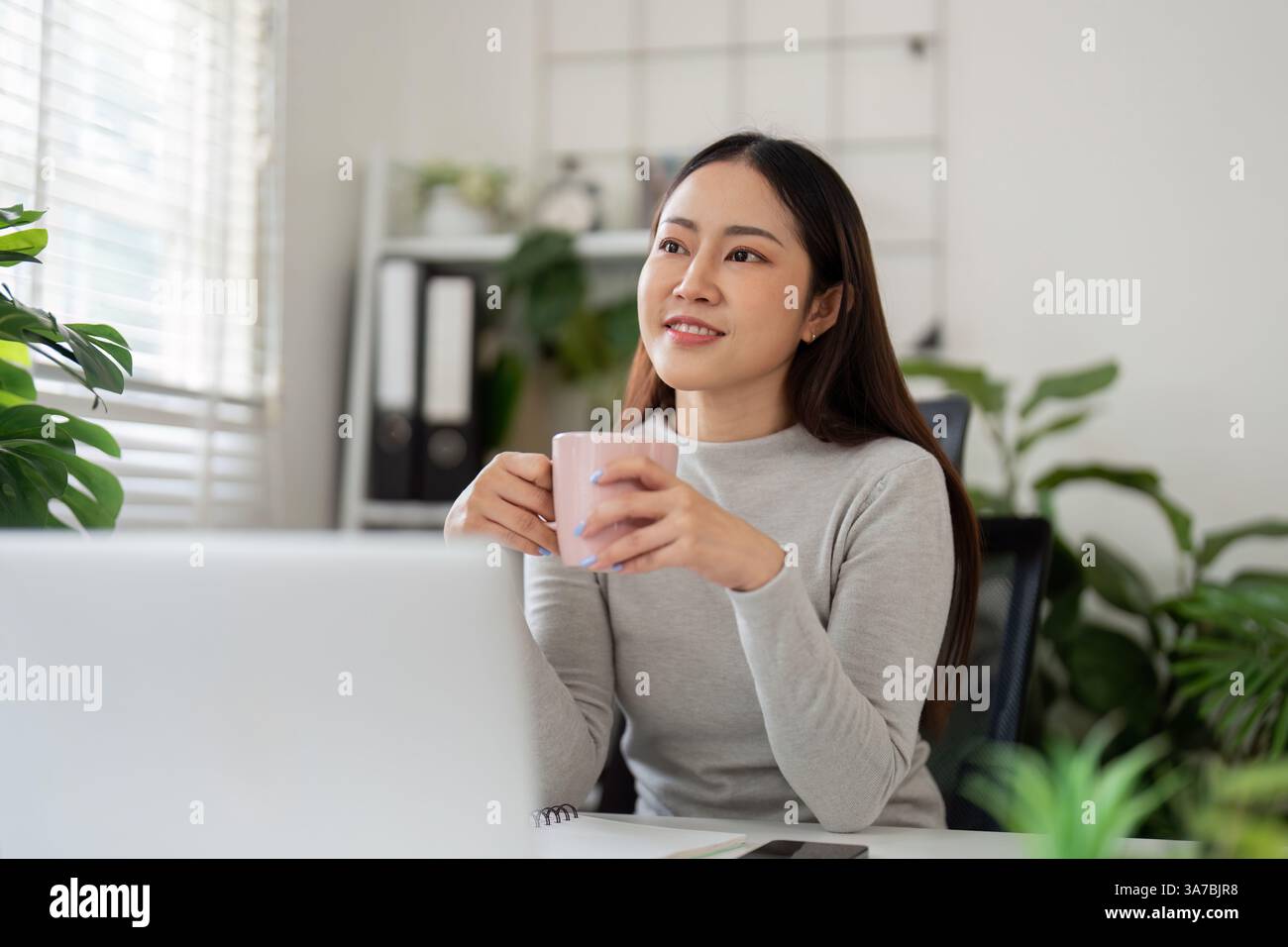Work and Productivity. A young woman enjoys a warm beverage while ...