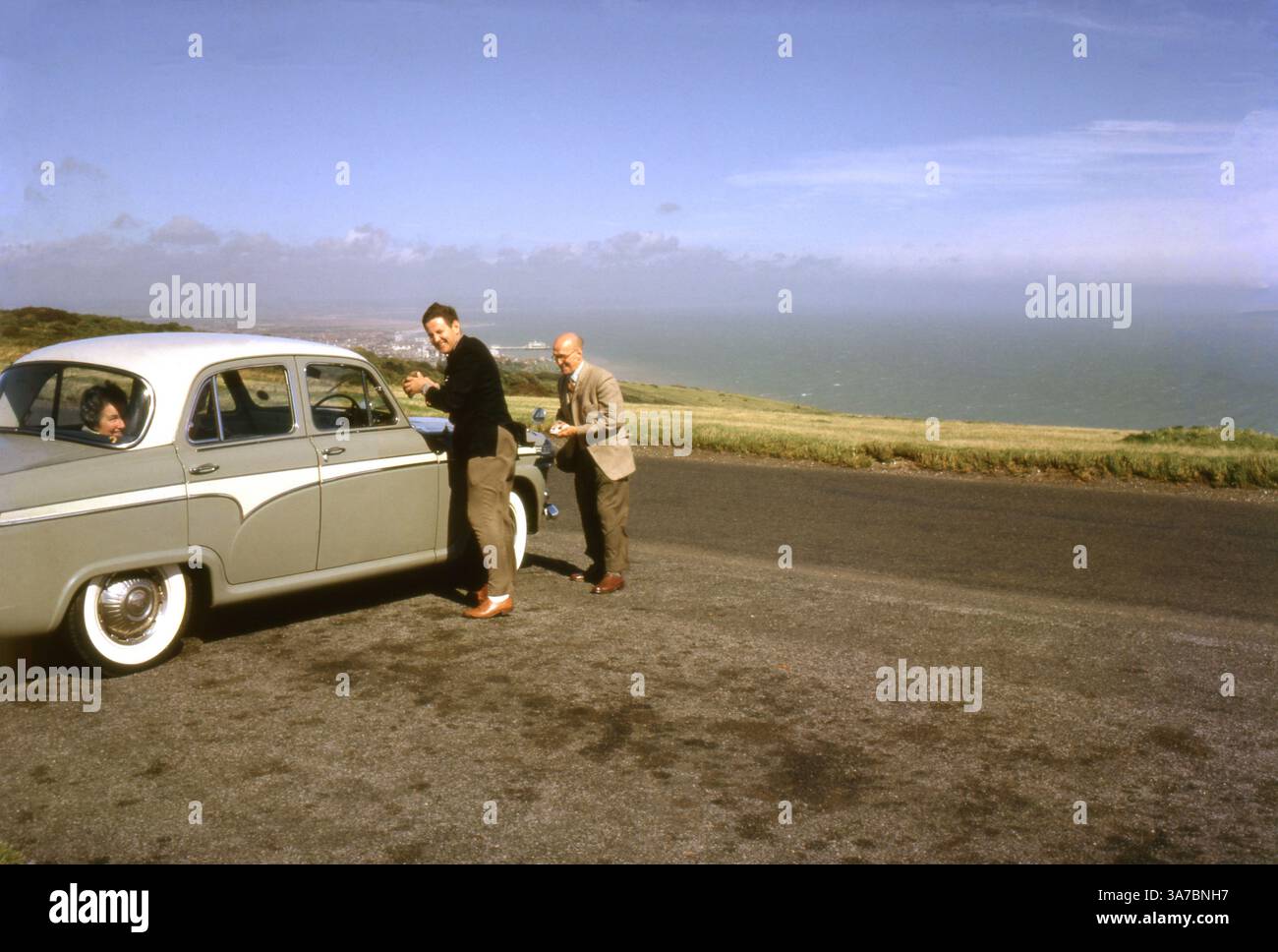A family returns to their classic car after a windy outing in the hills ...