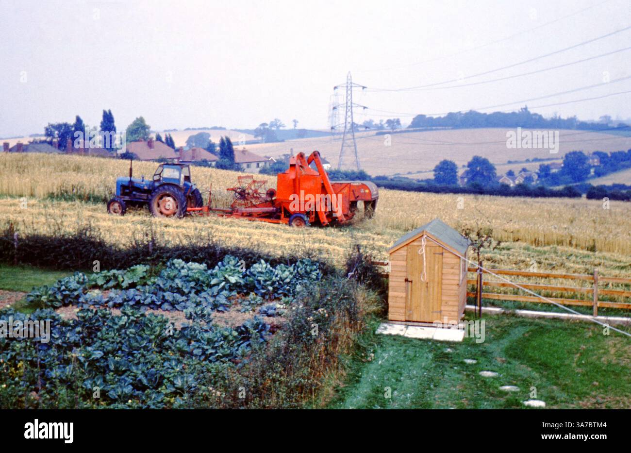 A classic 1960s British farming scene shows a blue Ford or Fordson ...