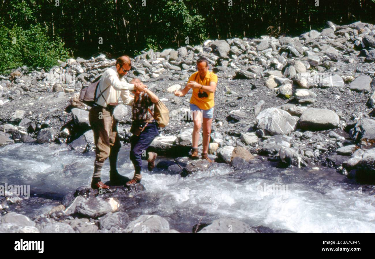 Three hikers help one another across a fast-flowing mountain stream in ...