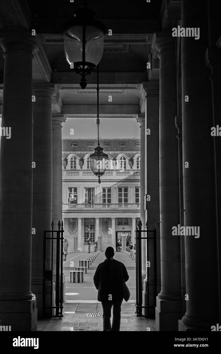 Silhouette of a person walking through columns of Palais Royal in Paris ...