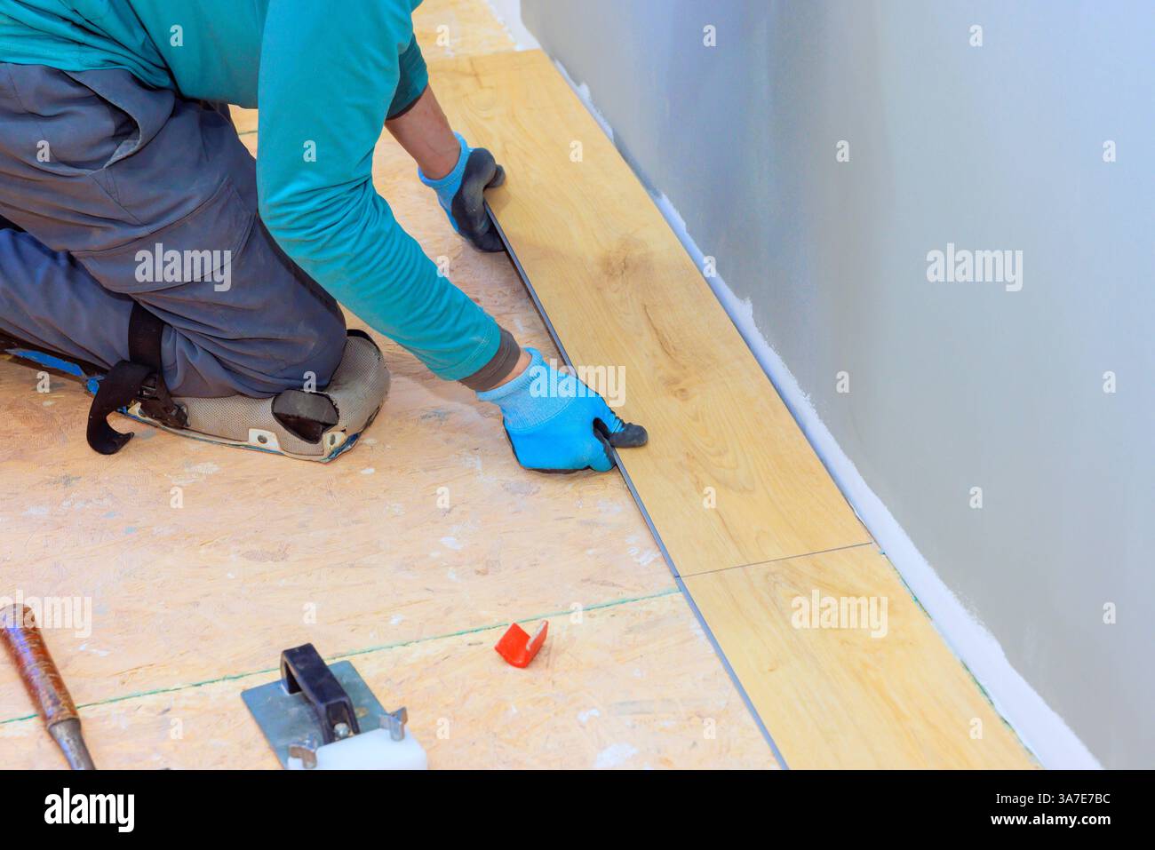 Contractor kneels on floor, carefully laying down new laminate flooring ...