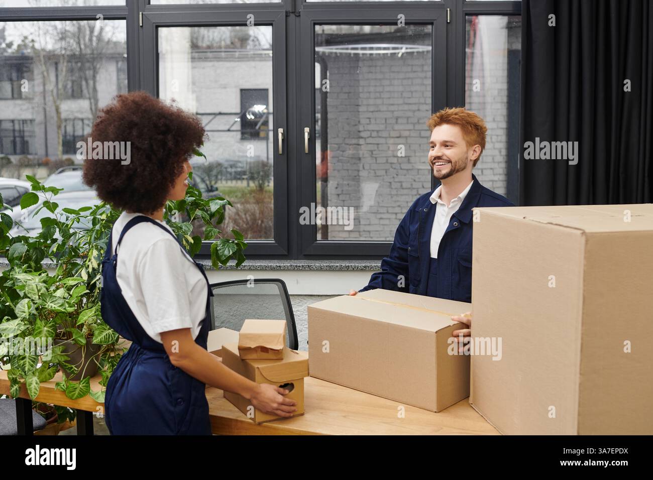 Two people pack and unpack boxes in a modern office filled with plants ...