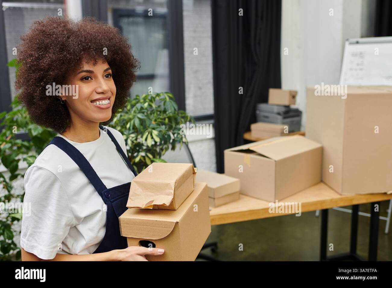 A young woman smiles as she carries packed boxes while preparing to ...