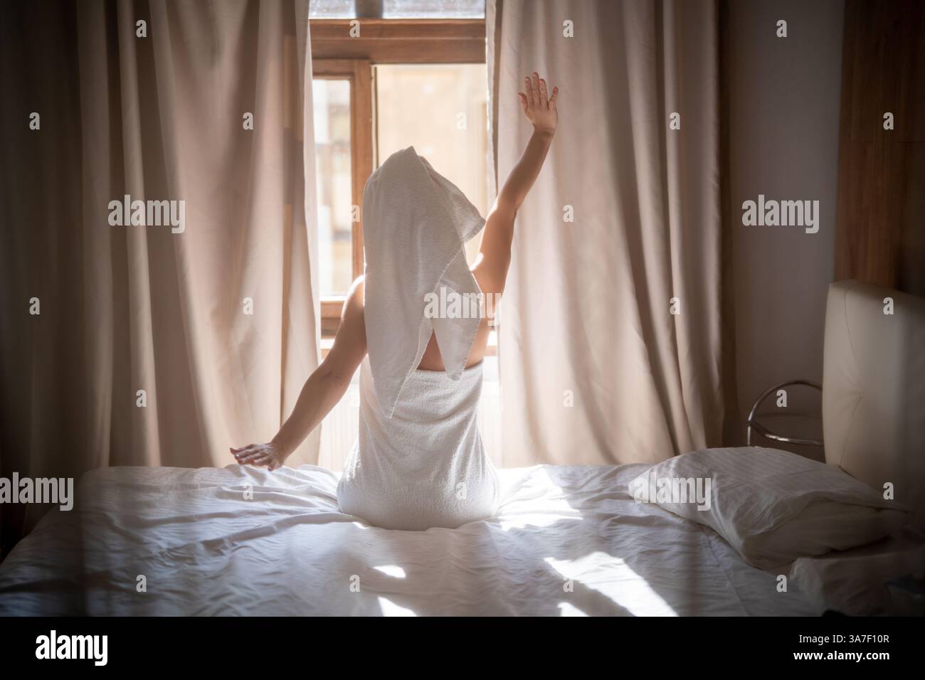 Back view of young woman in towel sitting on bed and meditating at ...