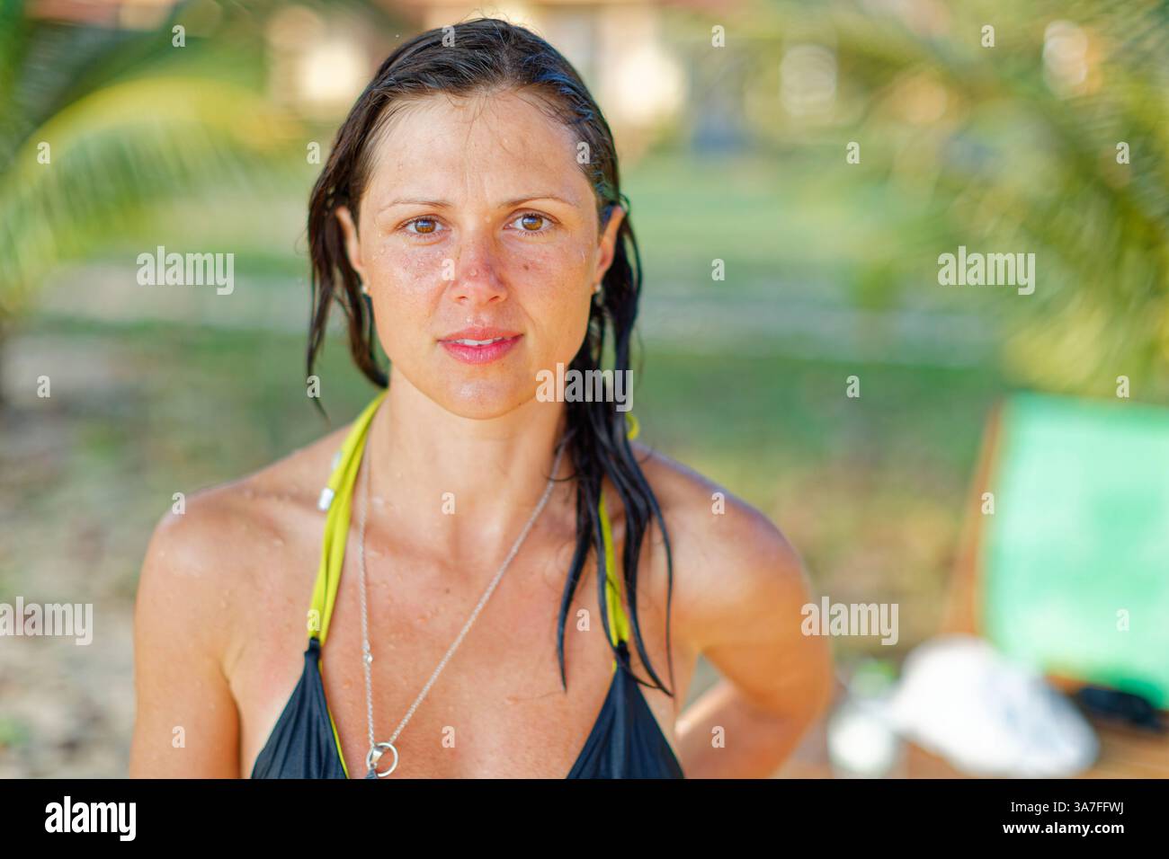 Close-up of joyful woman in swimsuit under tree, sea droplets on skin ...