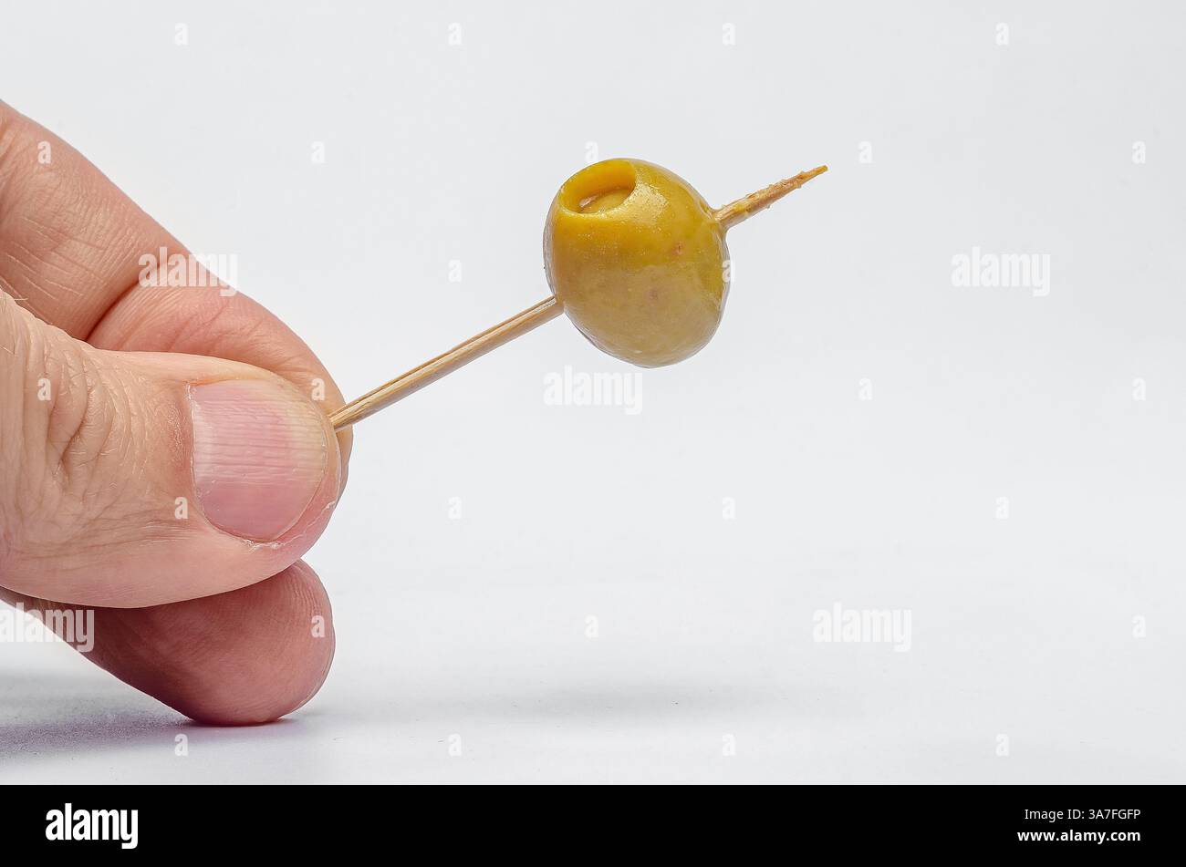Hand holding a single green olive on a toothpick against white ...