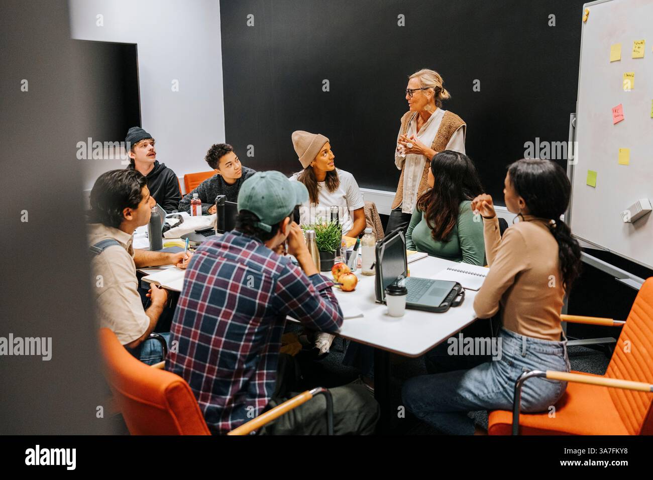 Mature female professor teaching multiracial students in classroom at ...