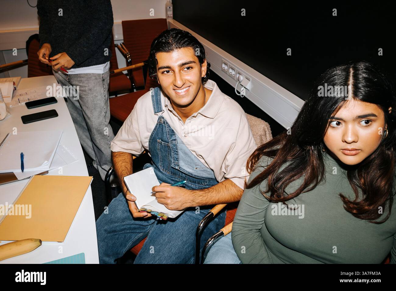 High angle view of smiling young man wearing bib overalls taking notes ...