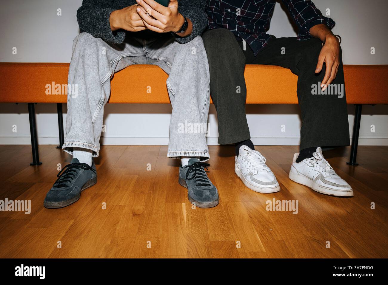 Low section of male friends sitting on sofa in tech university campus ...