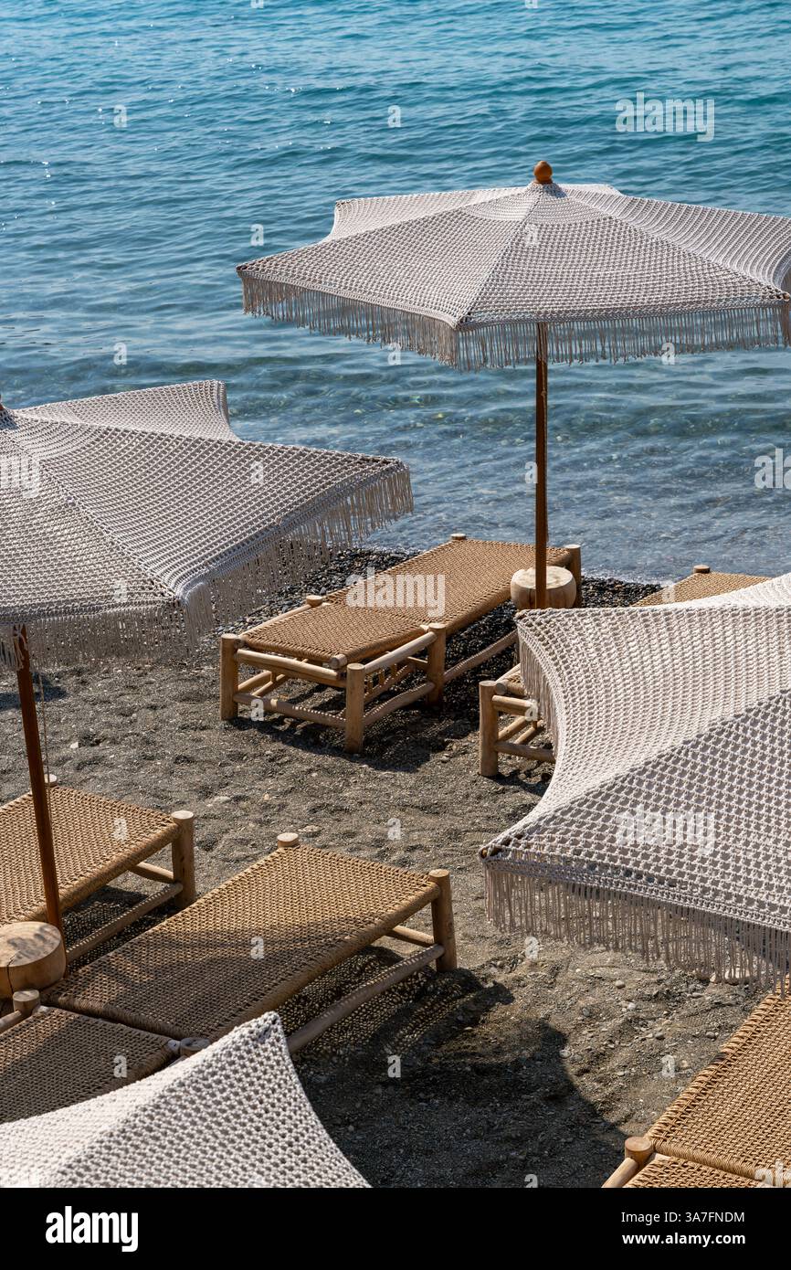 Idyllic Mediterranean beach with empty sun loungers and parasols under a thatched roof ...
