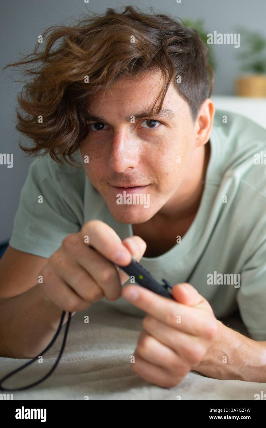 Portrait of handsome excited gamer lying on a bed and playing video ...