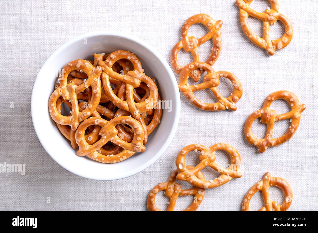 Salted pretzels in a white bowl on linen fabric. Golden toasted small ...