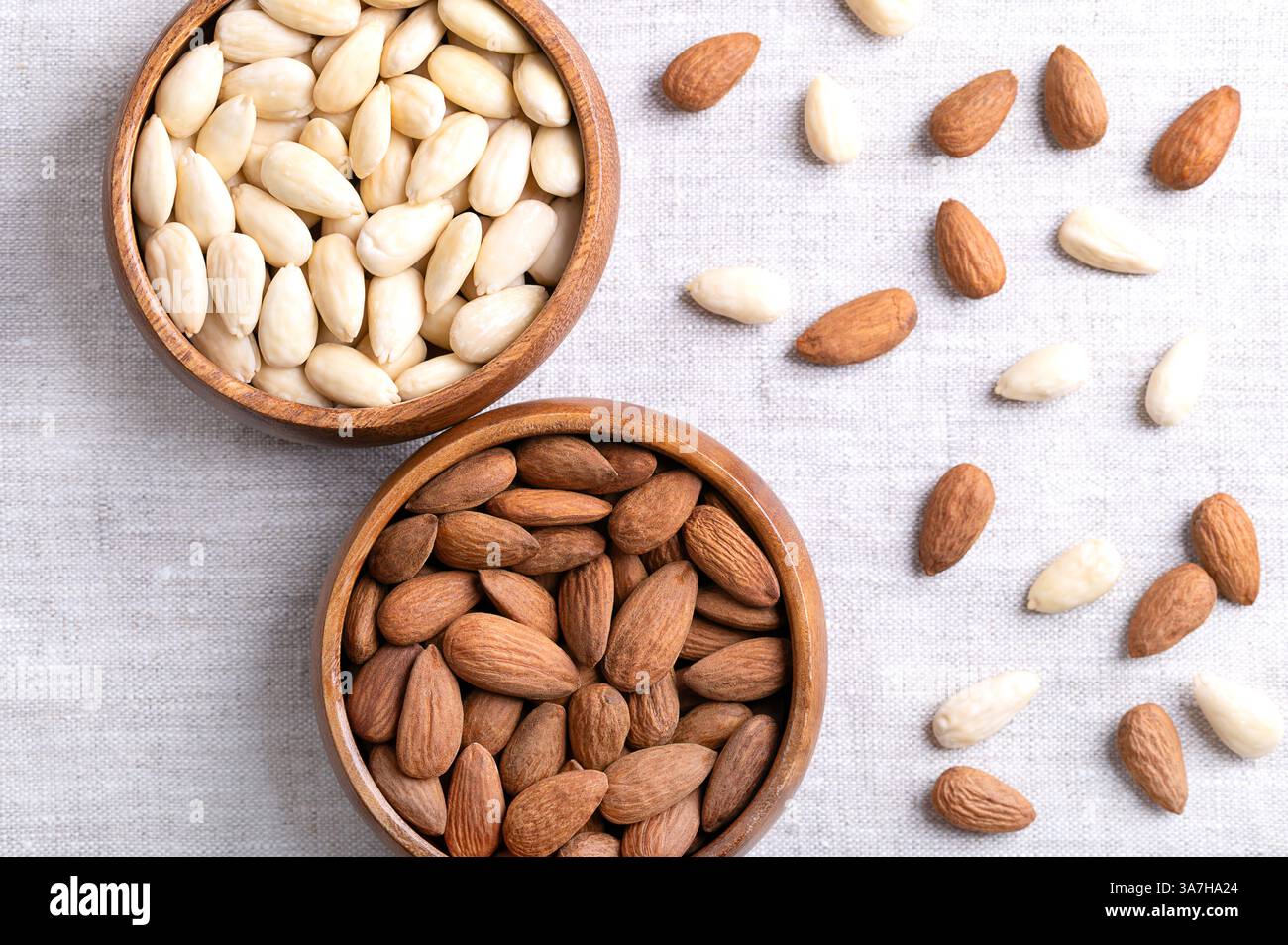Almonds, with seed coats and blanched, in wooden bowls, on linen fabric ...