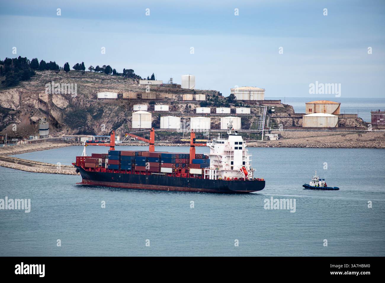 Container ship entering port near oil terminal Stock Photo - Alamy