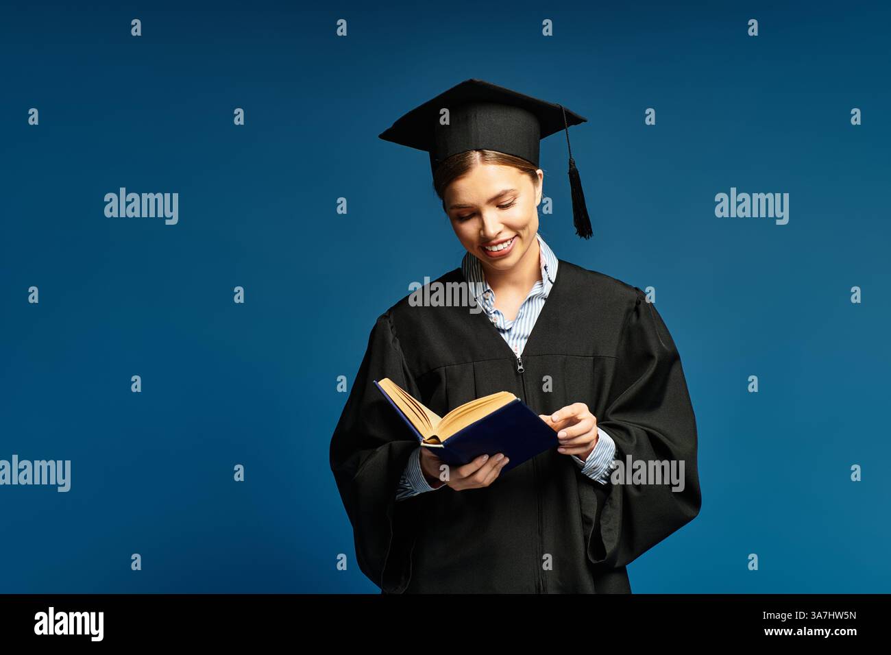 A joyful young woman in a graduation gown happily reads a book ...