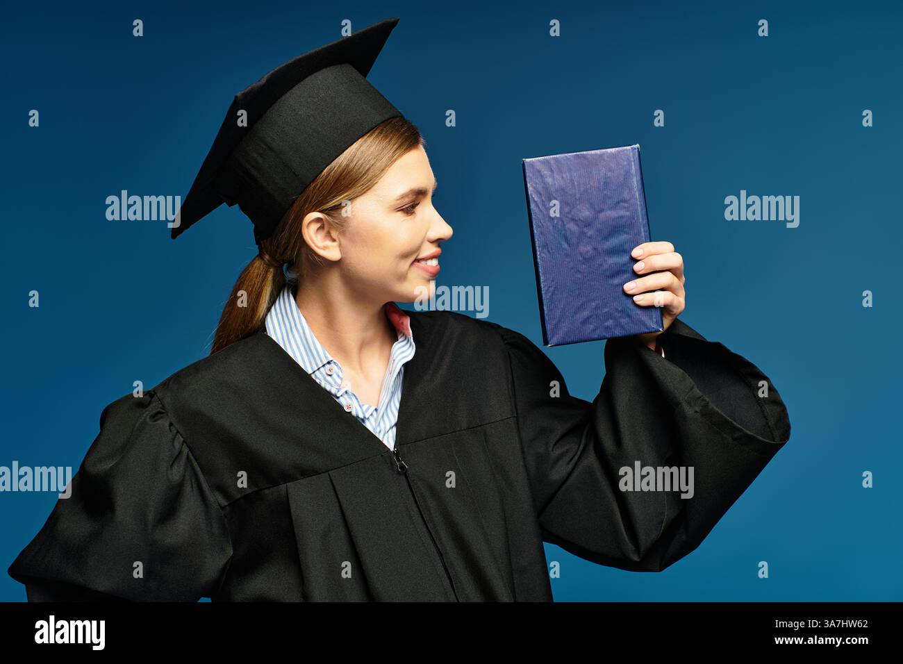 A happy young woman in a graduation gown proudly shows off her diploma ...