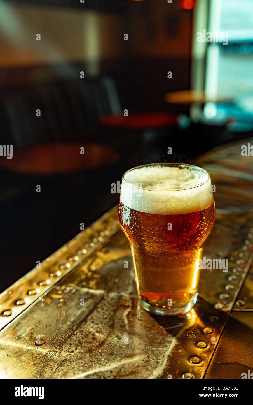 Amber beer with dense white foam sitting on rustic counter with ...