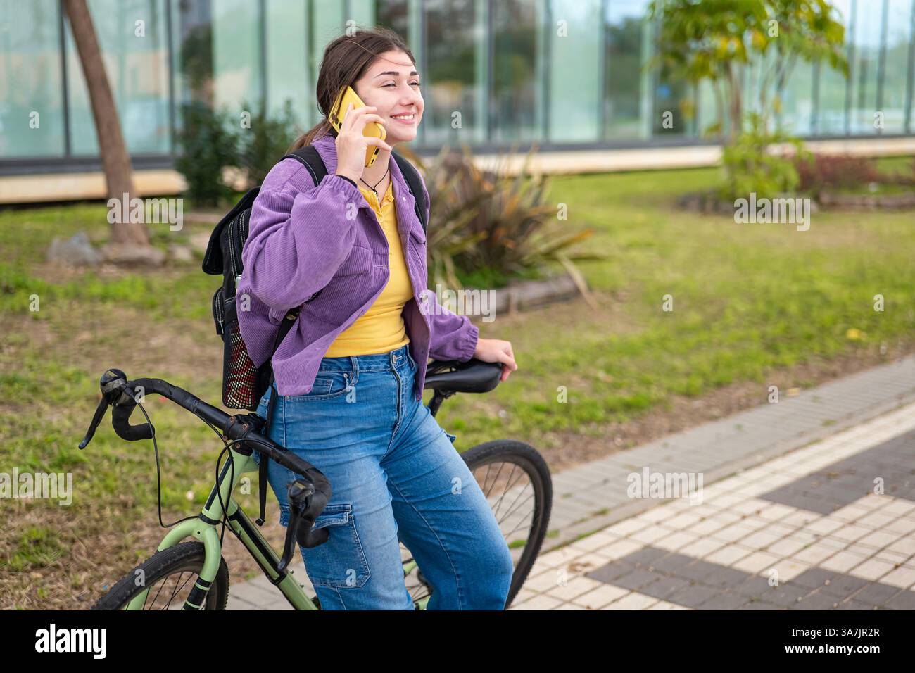 Young girl leaning on the bar of her bicycle, talking on her mobile ...
