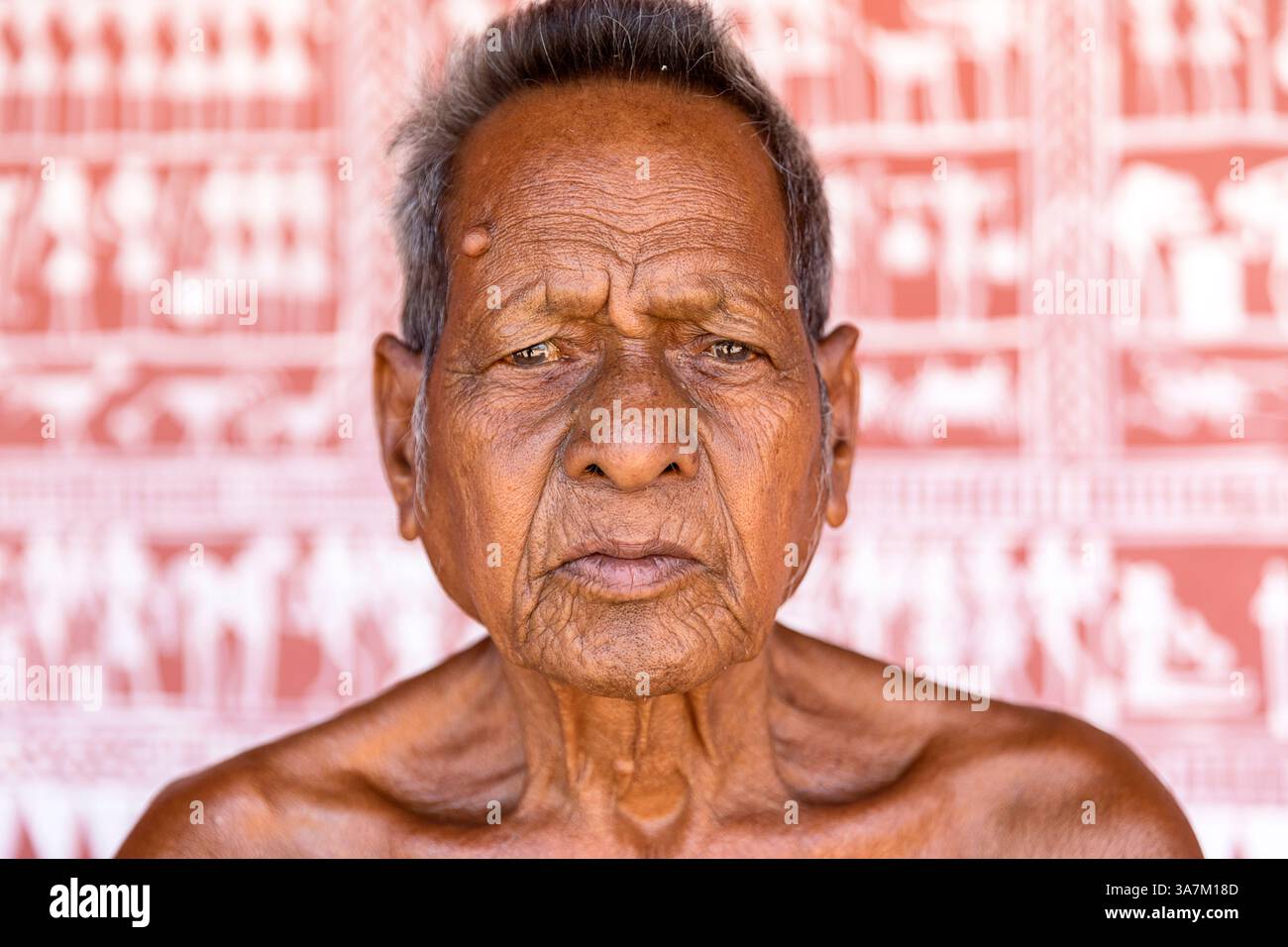 Portrait of a man from Lanjia Saura tribe sitting in front of a house ...