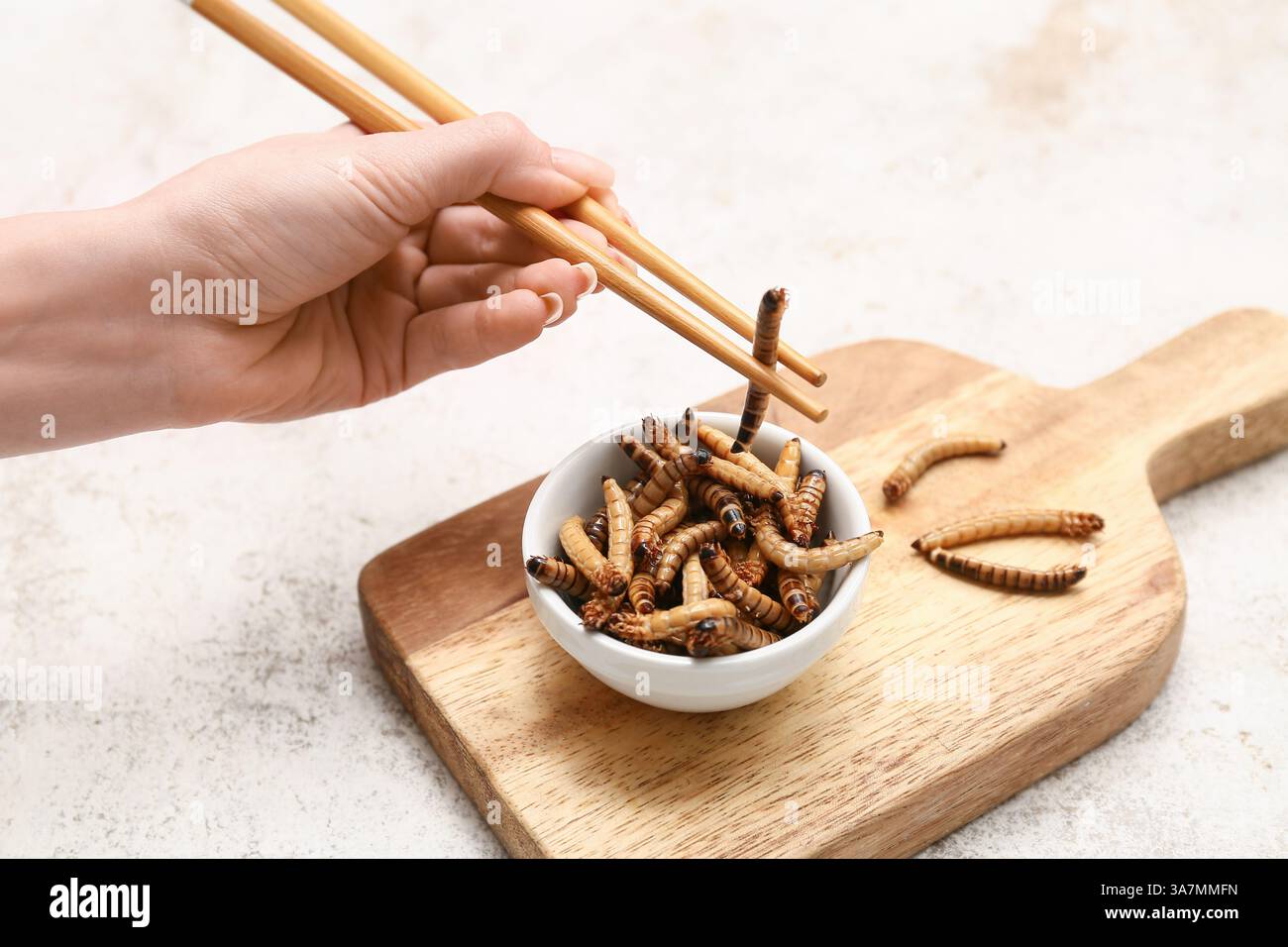 Female hand with chopsticks and bowl of fried maggots on white ...