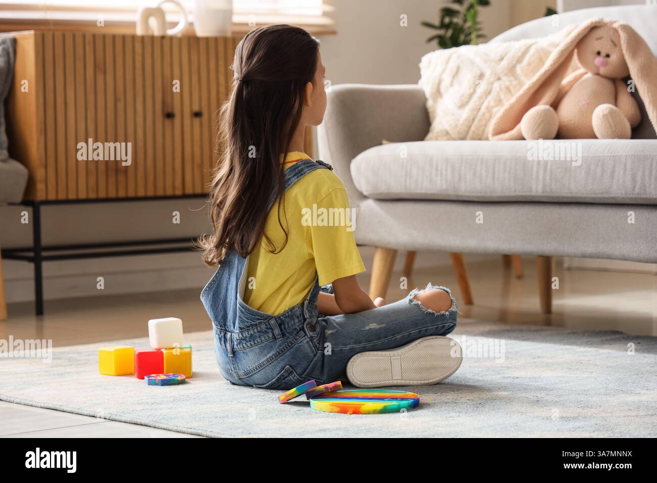 Cute girl with autistic disorder and toys sitting on floor at home ...