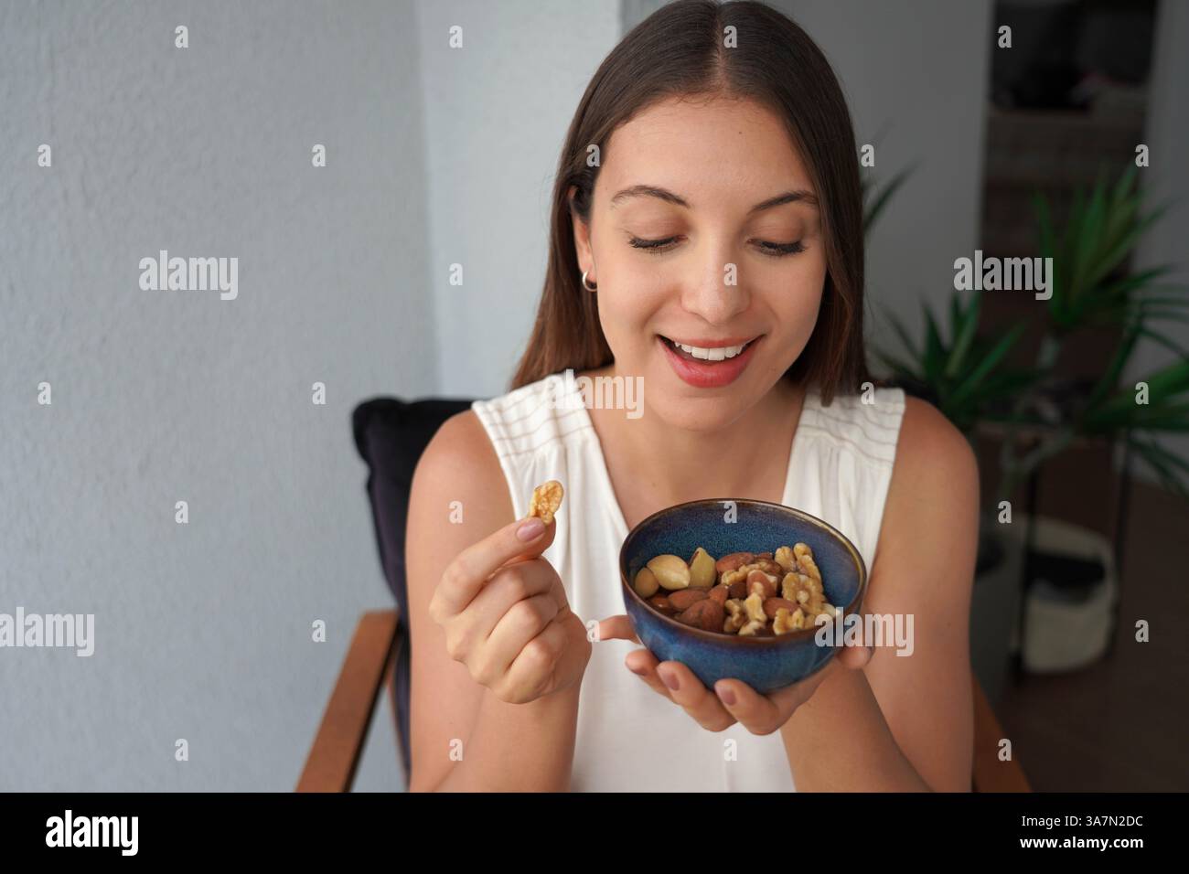 Pretty healthy girl picking mix of nuts dried fruits from bowl as snack ...