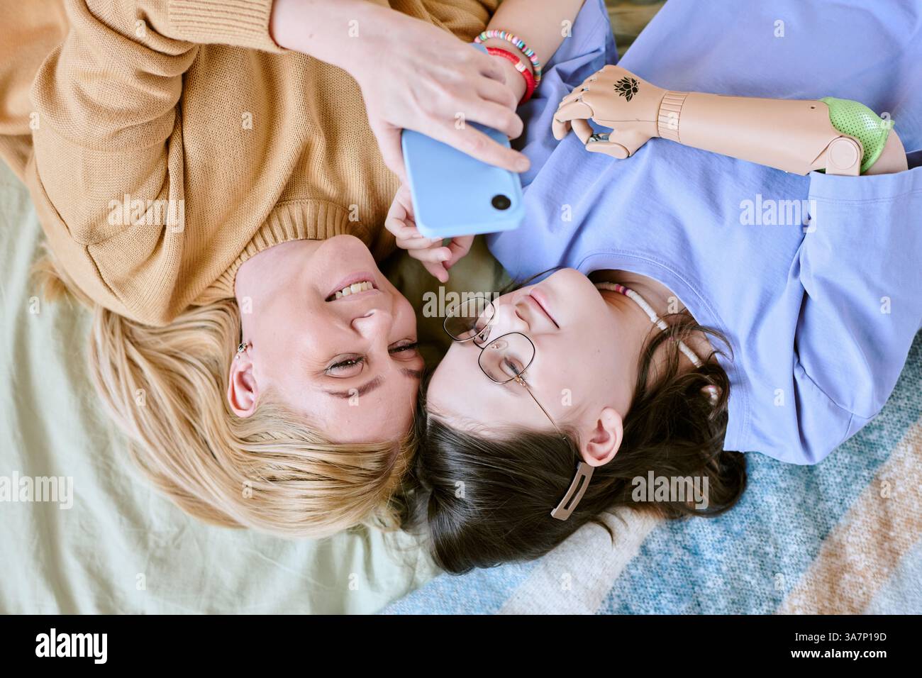 Close-up of mother and her daughter with prosthetic hand laying on bed ...