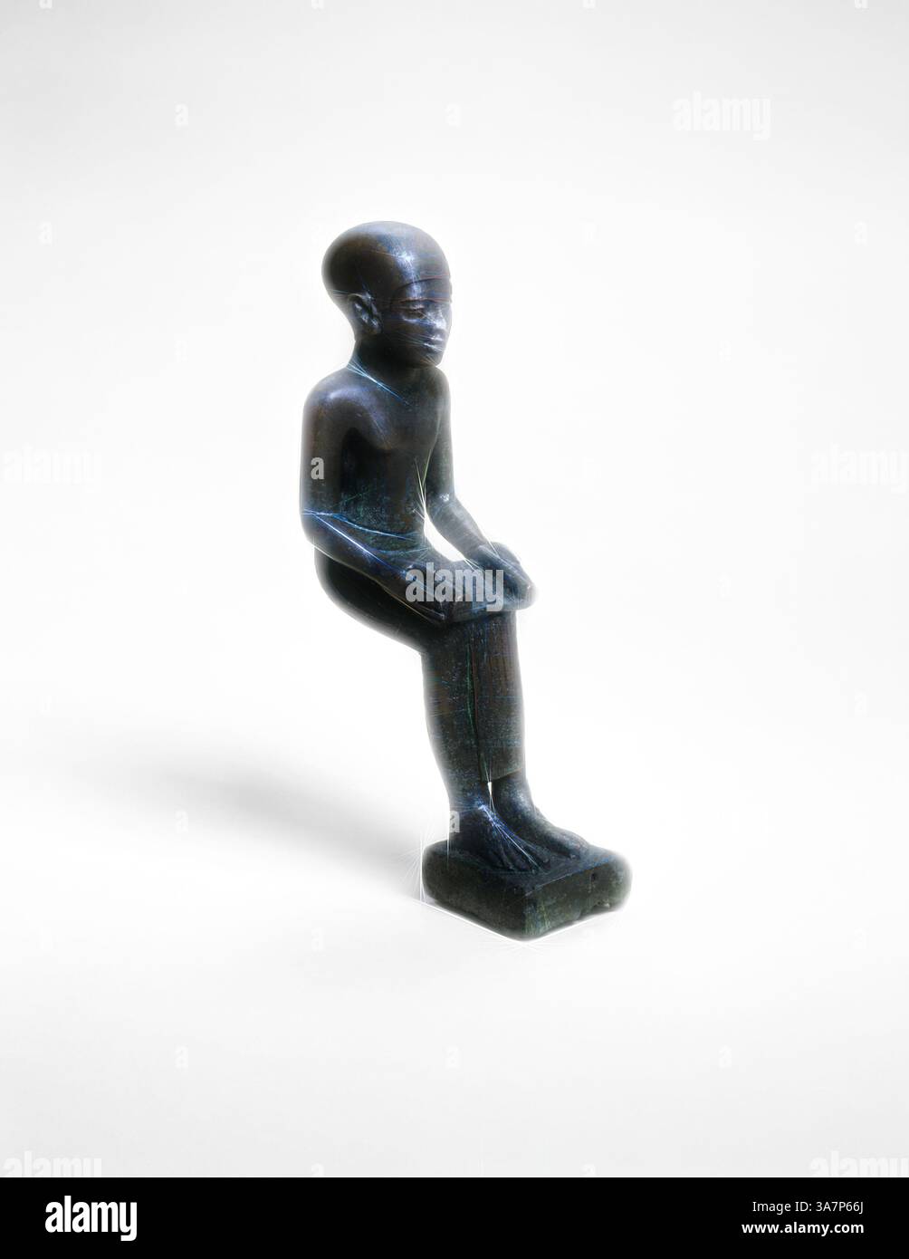 A seated figure carved from dark stone, depicting a humanoid form with ...