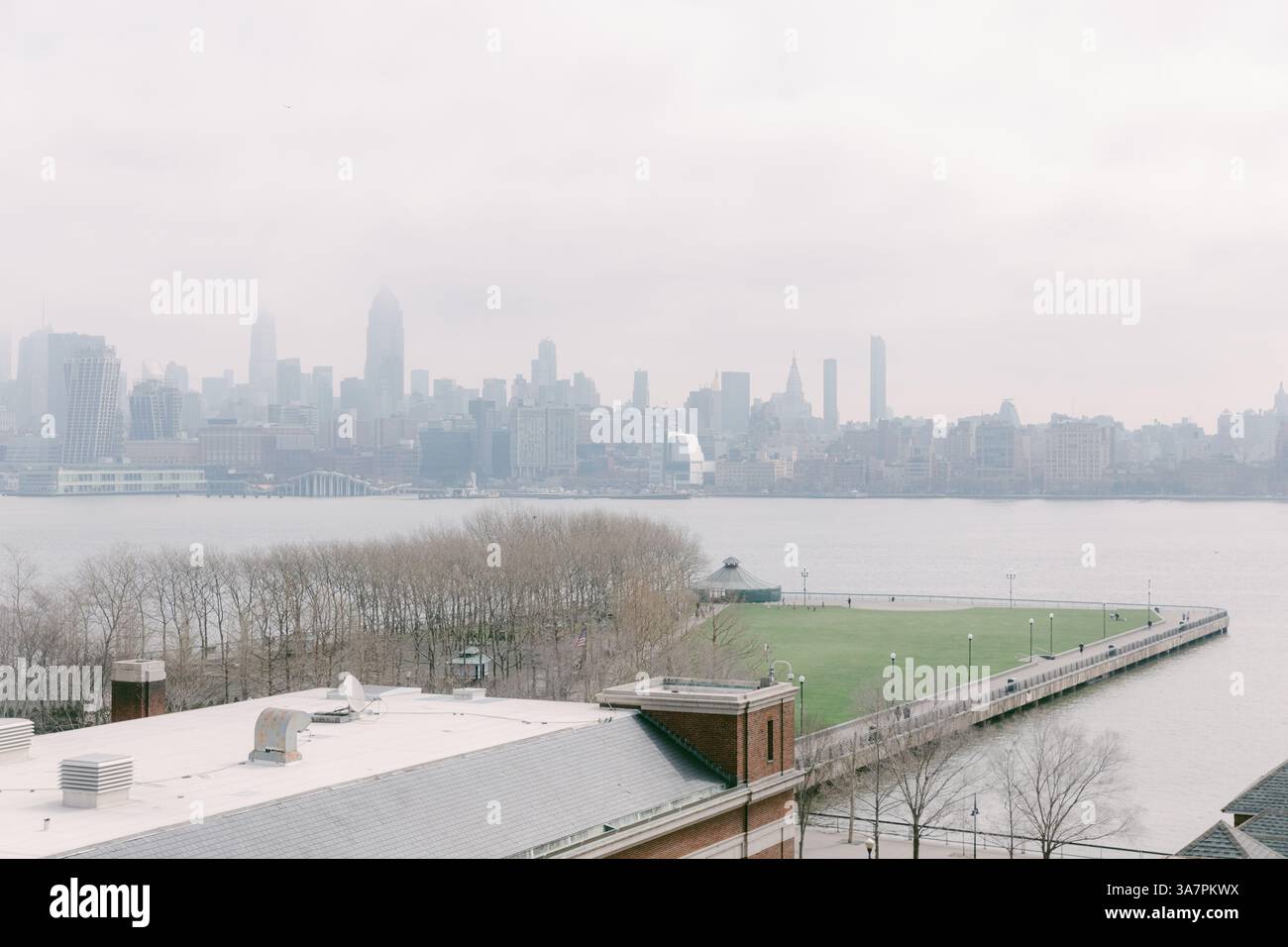 A muted city skyline stretches above a calm river, revealing park areas ...
