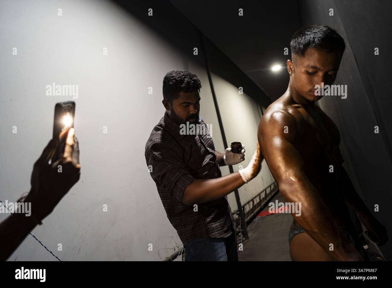 A male participant gets his body painted with tanning cream backstage ...