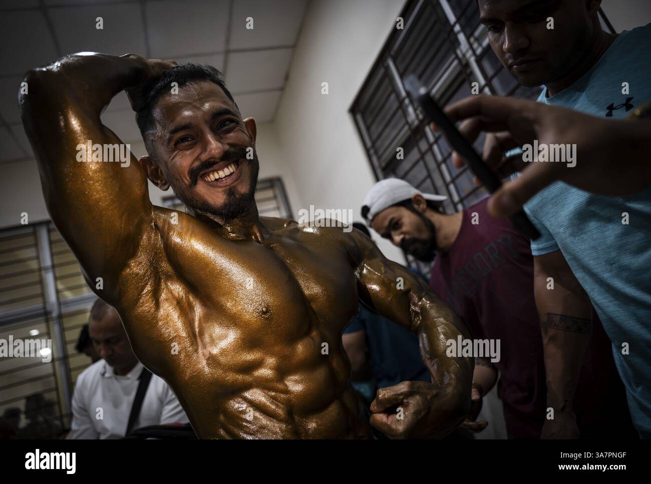 A male participant gets his body painted with tanning cream backstage ...