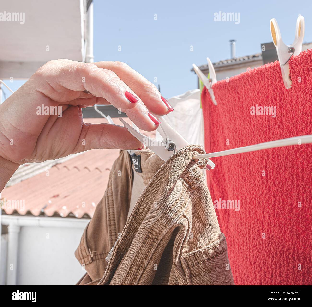 Hand hanging laundry on a clothesline under bright sunlight in a ...