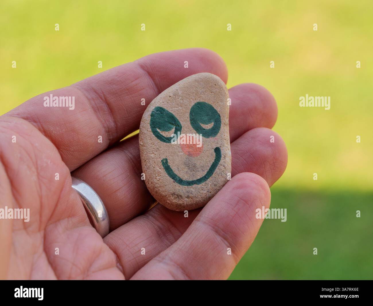 A hand grasps a stone adorned with a cheerful smiling face design Stock ...