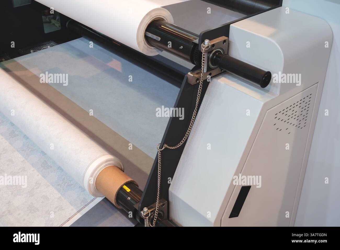 A roll of paper is being fed through a industrial printer machine. The ...