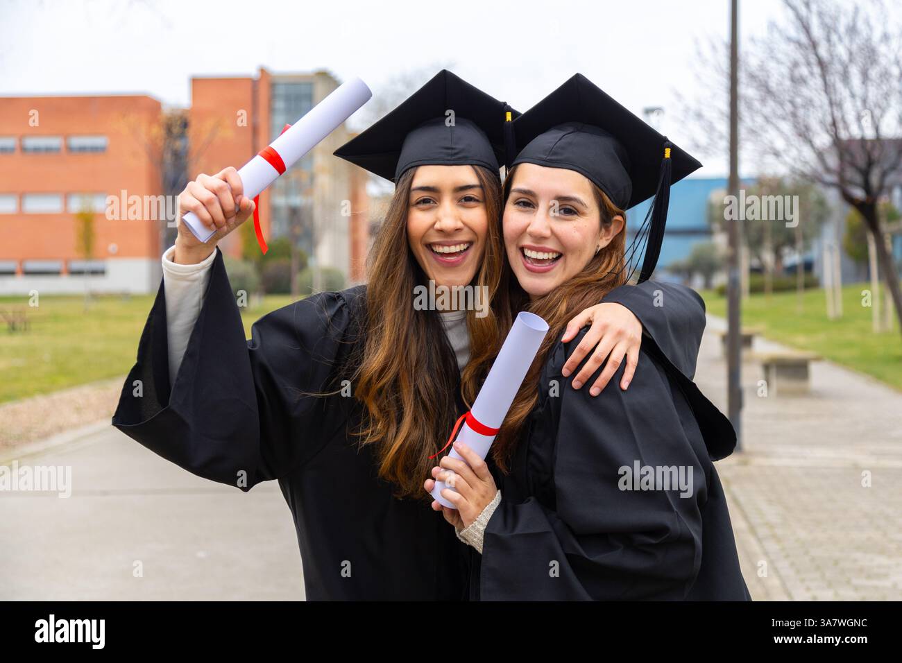 Two female students wearing graduation gowns and caps are happily ...