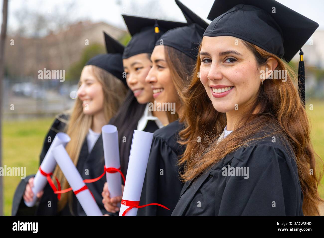 Group of multi ethnic female graduates wearing academic gowns and ...