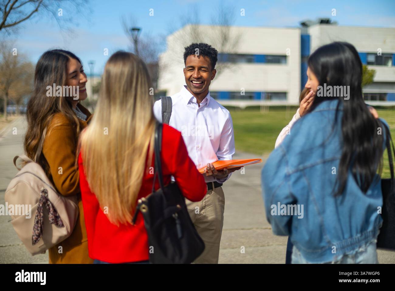 Happy teacher engaging with students on a university campus, holding a ...