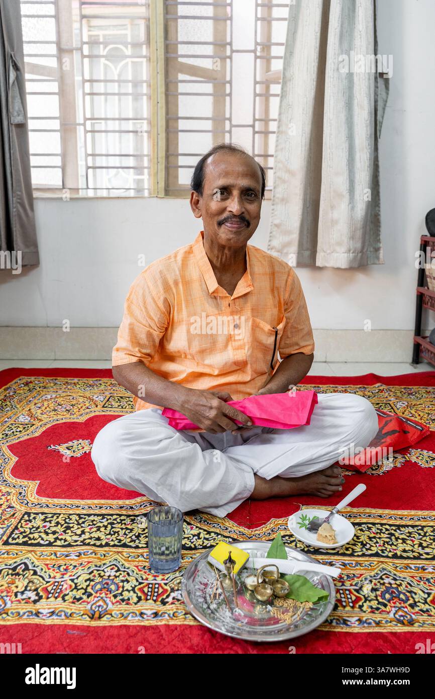 Indian hindu priest sitting on prayer mat, holding pink cloth ...