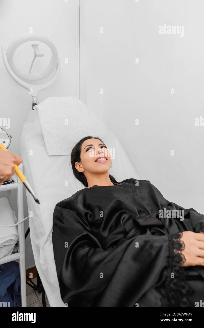 Latin American woman lying on a stretcher looking happily at her makeup ...