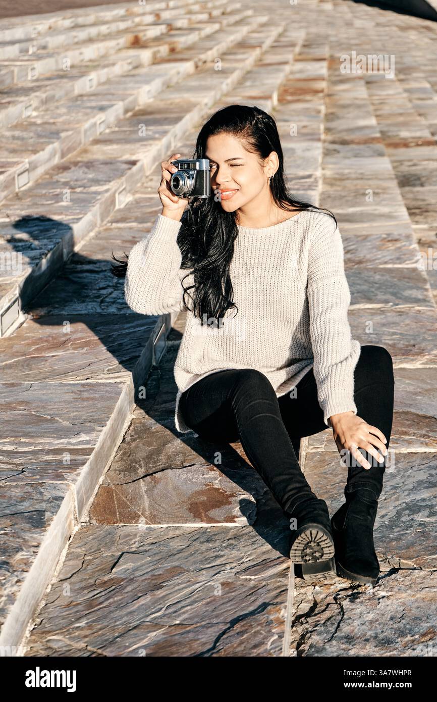 Optimistic ethnic female using photo camera to take pictures of street ...