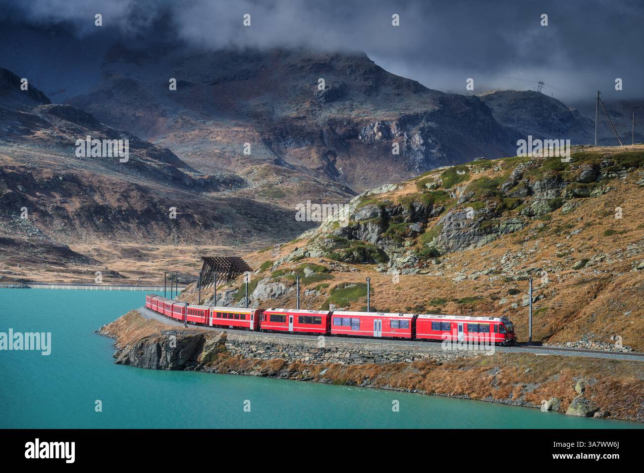 Aerial view of modern red train near azure mountain lake and dramatic ...